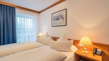 Quarto de hotel com duas camas, mesa de cabeceira com luminária e telefone, pintura na parede e janela com cortinas.