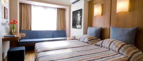 Quarto de hotel com duas camas, um sofá, uma mesa e uma janela com cortinas.