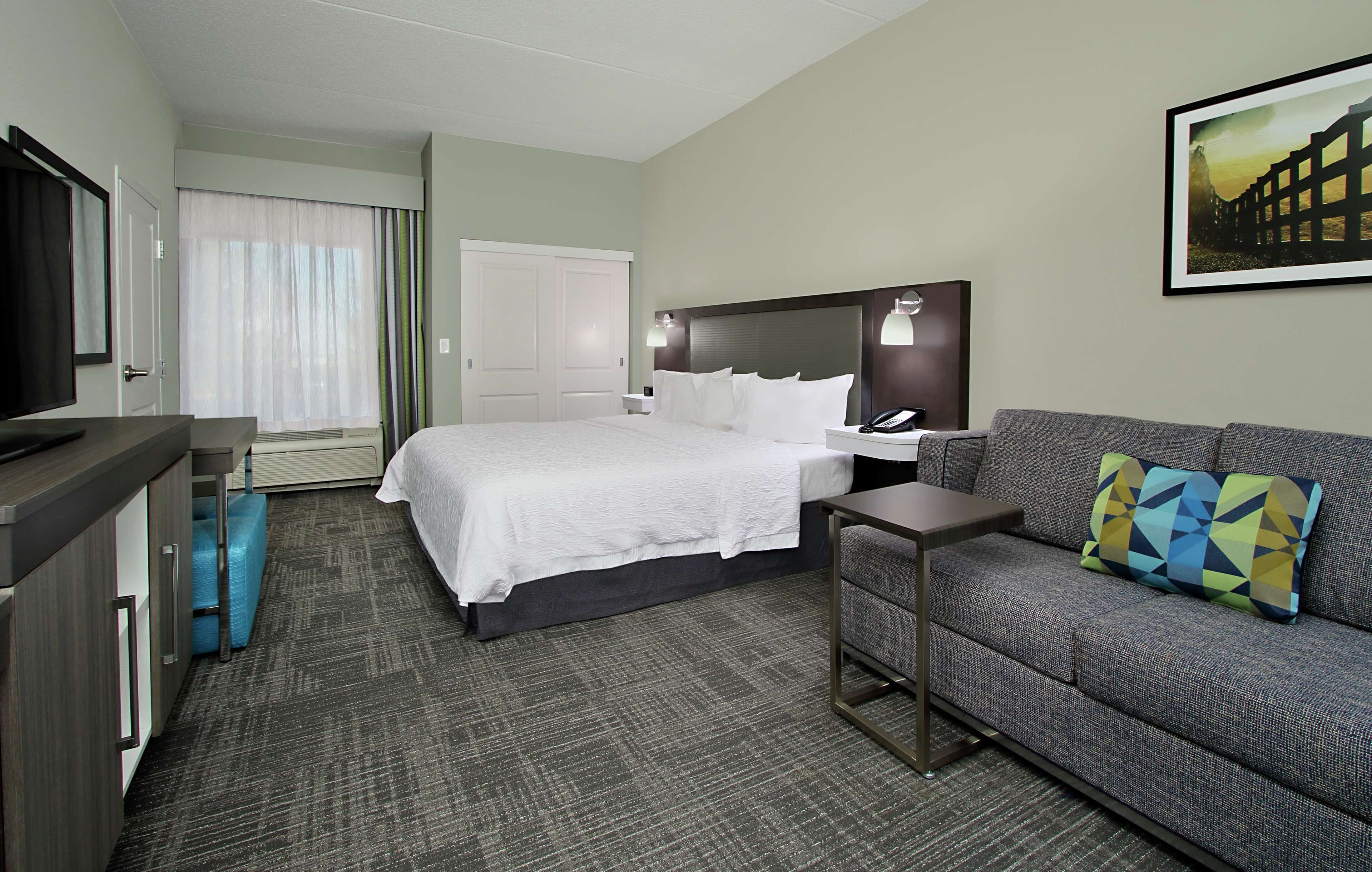 Quarto de hotel com cama, sofá, televisão e escrivaninha.