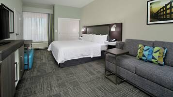 Quarto de hotel com cama, sofá, televisão e escrivaninha.
