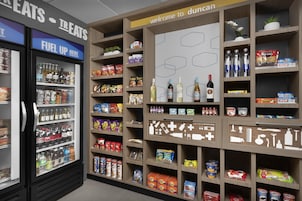 Uma área com lanches e bebidas, com prateleiras cheias de diversos petiscos, refrigerantes e produtos de higiene pessoal.