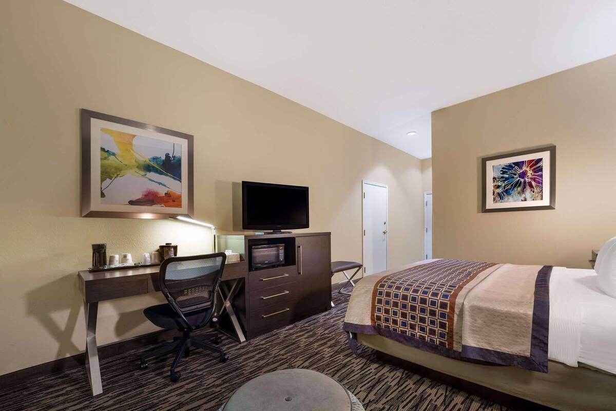 Quarto de hotel com cama, escrivaninha, cadeira, televisão, micro-ondas e obras de arte nas paredes.