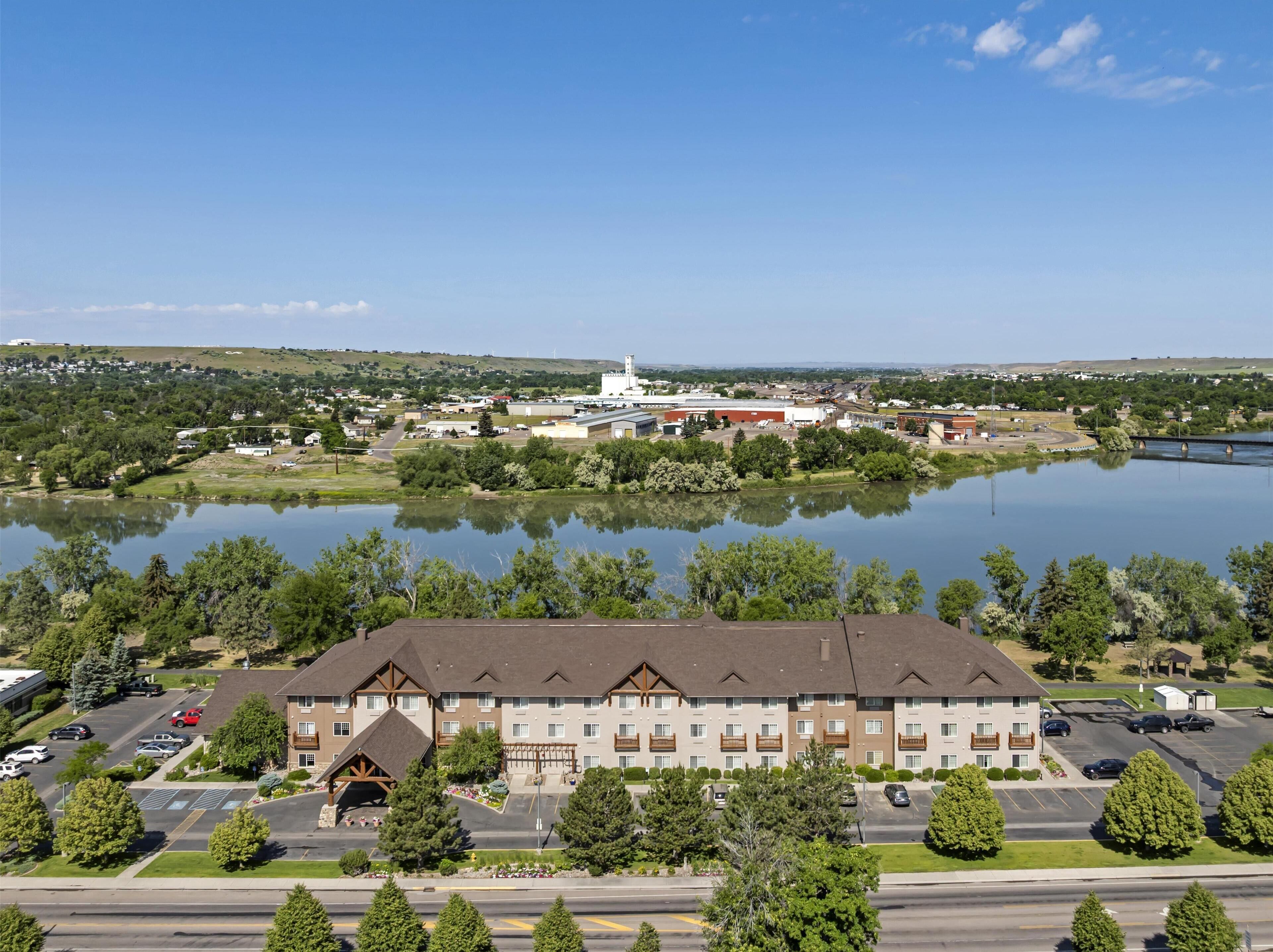 Um hotel grande com um pátio central e vista para um lago e edifícios industriais ao fundo.