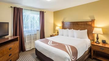 Quarto de hotel com cama, televisão, secretária, candeeiro e janela com cortinas.