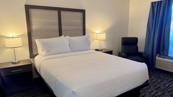 Quarto de hotel com uma cama grande, duas luminárias de cabeceira, uma cadeira e uma janela com cortinas.