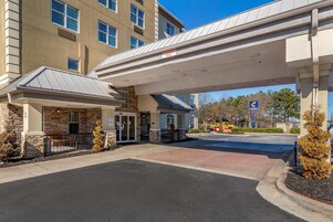 Entrada de hotel com galeria coberta, fachada de pedra e estacionamento com vaga acessível.