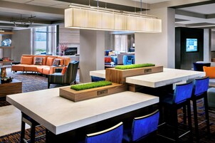 Um hall de hotel moderno com área de bar, assentos e uma tela de televisão.