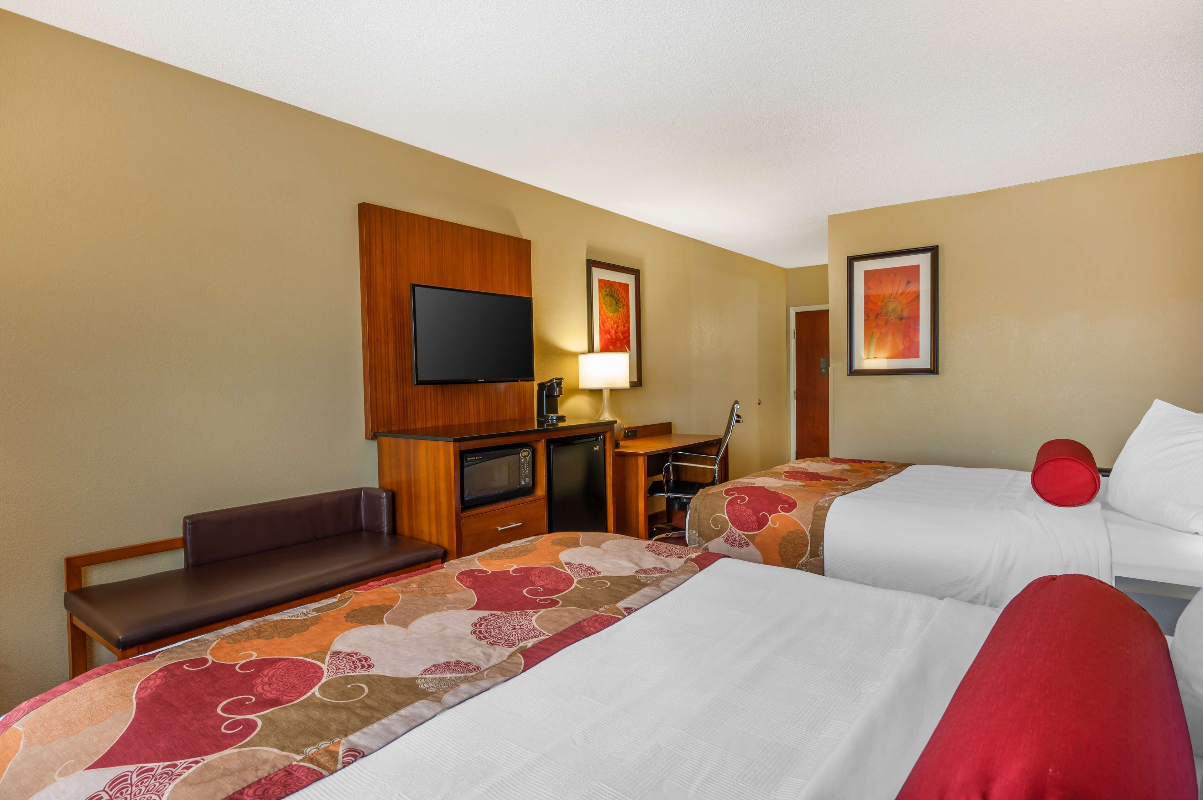 Quarto de hotel com duas camas, uma escrivaninha, uma televisão e uma pequena cozinha equipada.