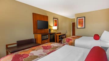 Quarto de hotel com duas camas, uma escrivaninha, uma televisão e uma pequena cozinha equipada.
