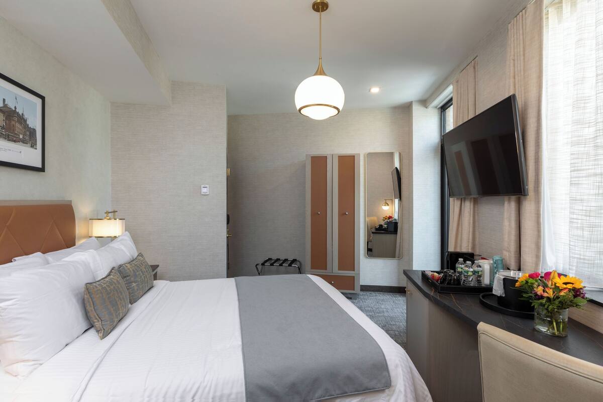 Quarto de hotel com cama, escrivaninha com televisão de tela plana, espelho e janela com cortinas.