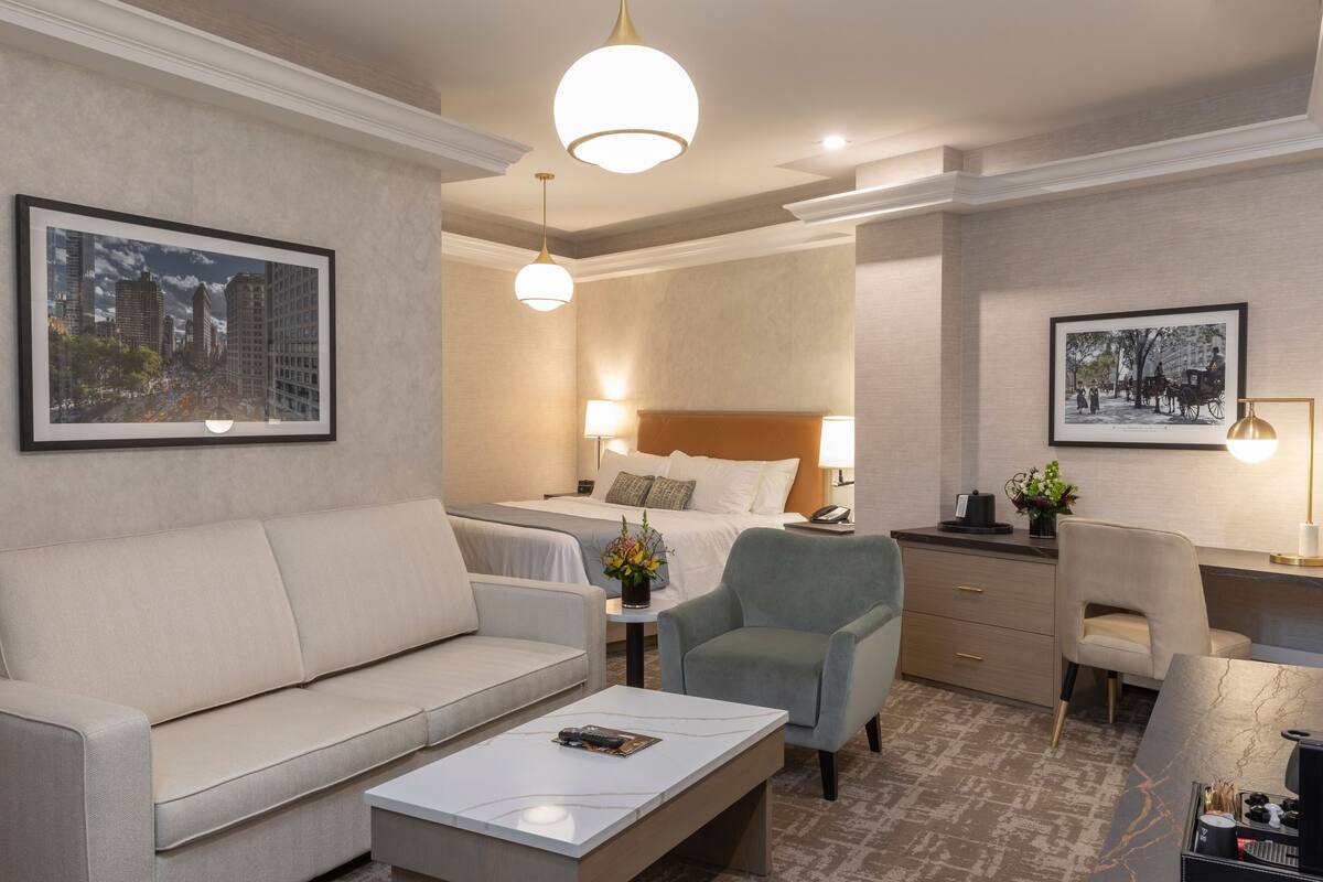 Quarto de hotel com sofá, duas camas de solteiro, escrivaninha e uma cadeira.