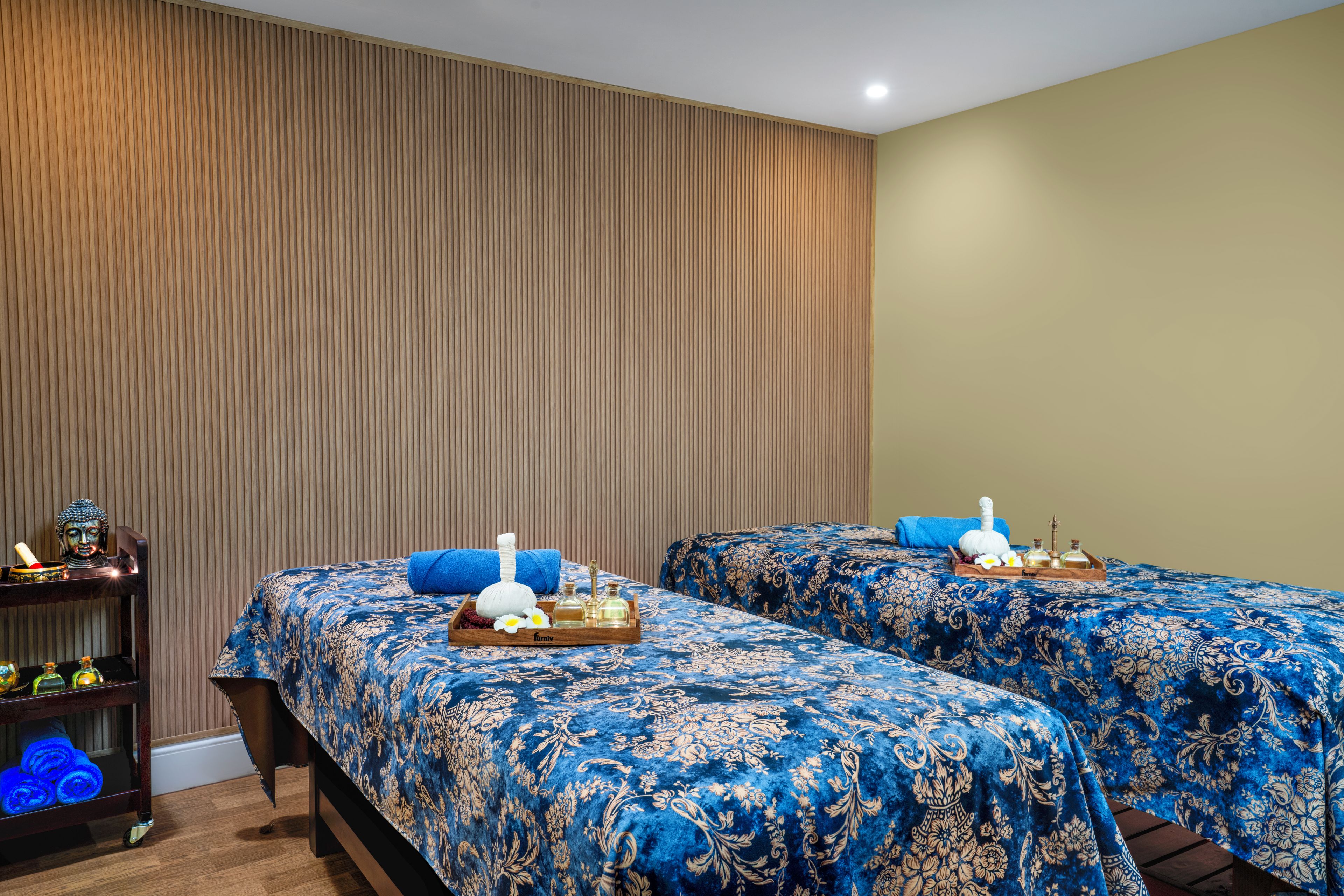 Quarto com duas camas, parede de painel de madeira e prateleira com toalhas e uma estátua de Buda.