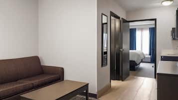 Quarto de hotel com sofá, mesinha, porta para um quarto e banheiro.