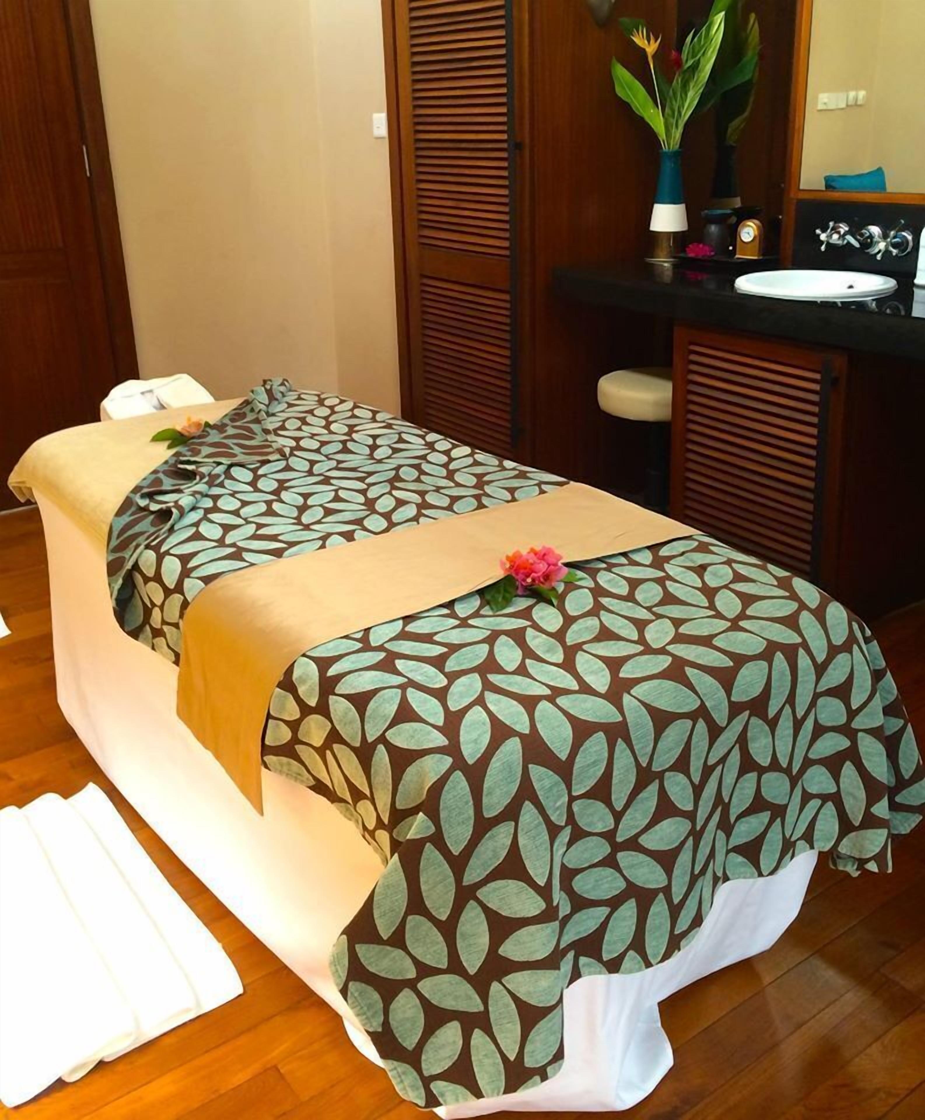 Uma mesa de massagem com capa estampada, uma plantinha no balcão e um espelho em cima.