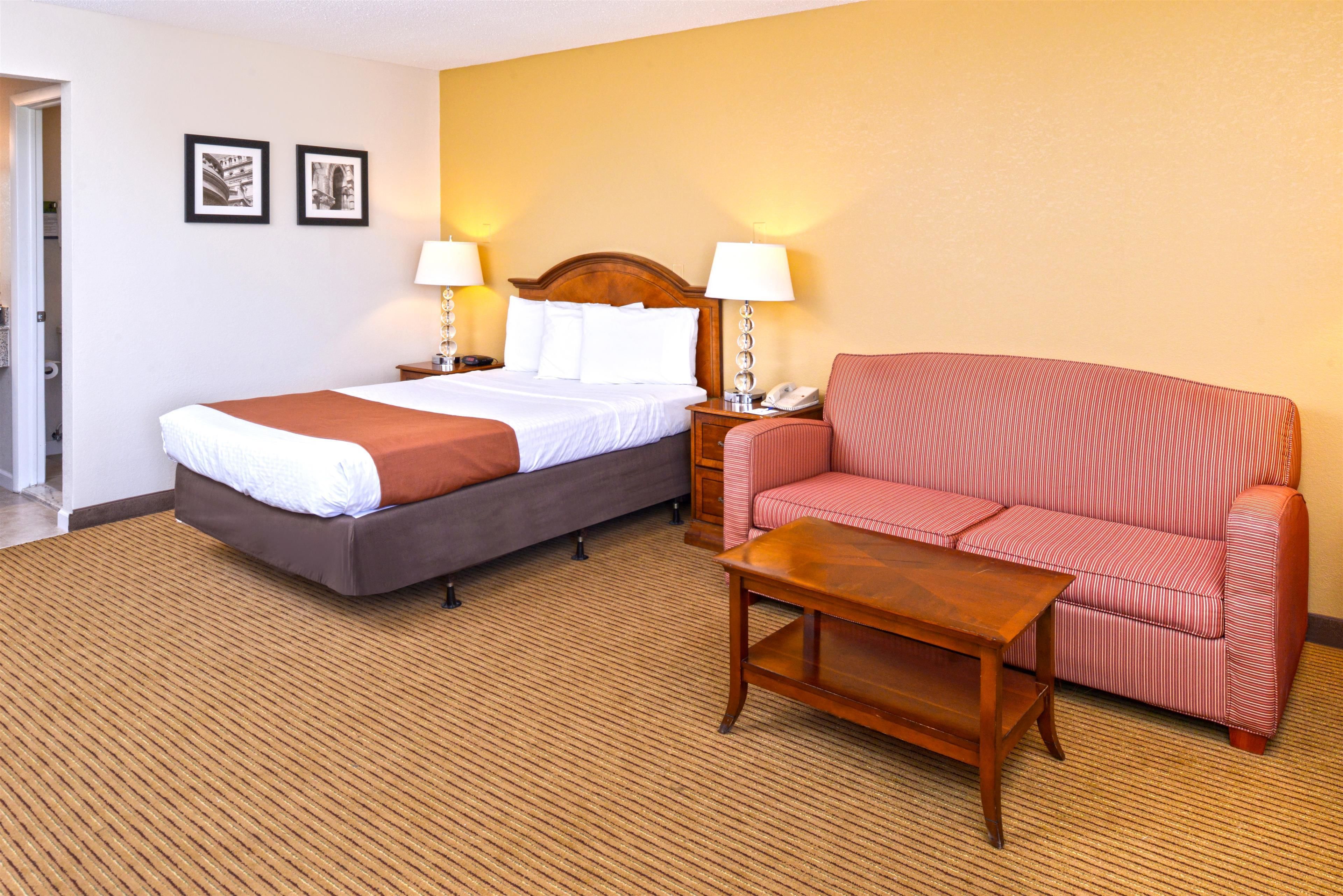 Quarto de hotel com cama, sofá, mesa de centro e duas luminárias.
