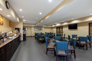 Um espaço de refeições de hotel com várias mesas e cadeiras, um balcão de buffet e uma televisão na parede.