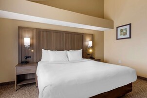 Quarto de hotel com uma cama grande, duas mesas de cabeceira com luminárias, uma mesinha de apoio e um quadro na parede.