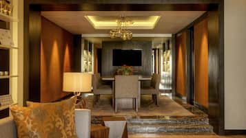 Um saguão moderno de hotel com área de refeições, uma TV de tela plana e um candelabro.