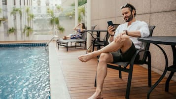 Um homem sentado em uma espreguiçadeira à beira da piscina, segurando um smartphone.