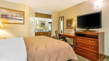 Quarto de hotel com cama, televisão, cômoda, escrivaninha e espelho.