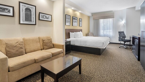 Quarto de hotel com cama, sofá, escrivaninha e quadros nas paredes.