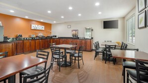 Uma cozinha moderna com armários de madeira, uma área de jantar com mesas e cadeiras, e uma TV de tela plana fixada na parede.