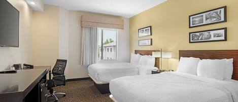 Quarto de hotel com duas camas, uma escrivaninha, uma cadeira e uma televisão.