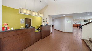 Uma área de recepção de hotel com um balcão de madeira, uma parede amarela e uma escada que leva ao andar superior.