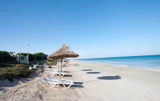 Na praia, espreguiçadeiras, guarda-sóis, prática de vôlei de praia 