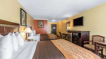 Quarto de hotel com uma cama grande, uma mesa de trabalho com cadeira, televisão e abajur.