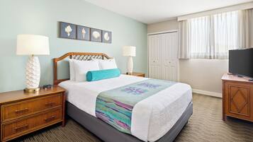 Quarto de hotel com uma cama, duas mesas de cabeceira, uma televisão, um guarda-roupa e uma janela com cortinas.