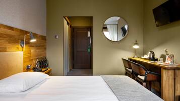 Quarto de hotel com cama, escrivaninha, cadeira e televisão na parede.