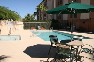 Uma área de piscina com mesa e cadeiras, um guarda-sol verde e uma cerca.