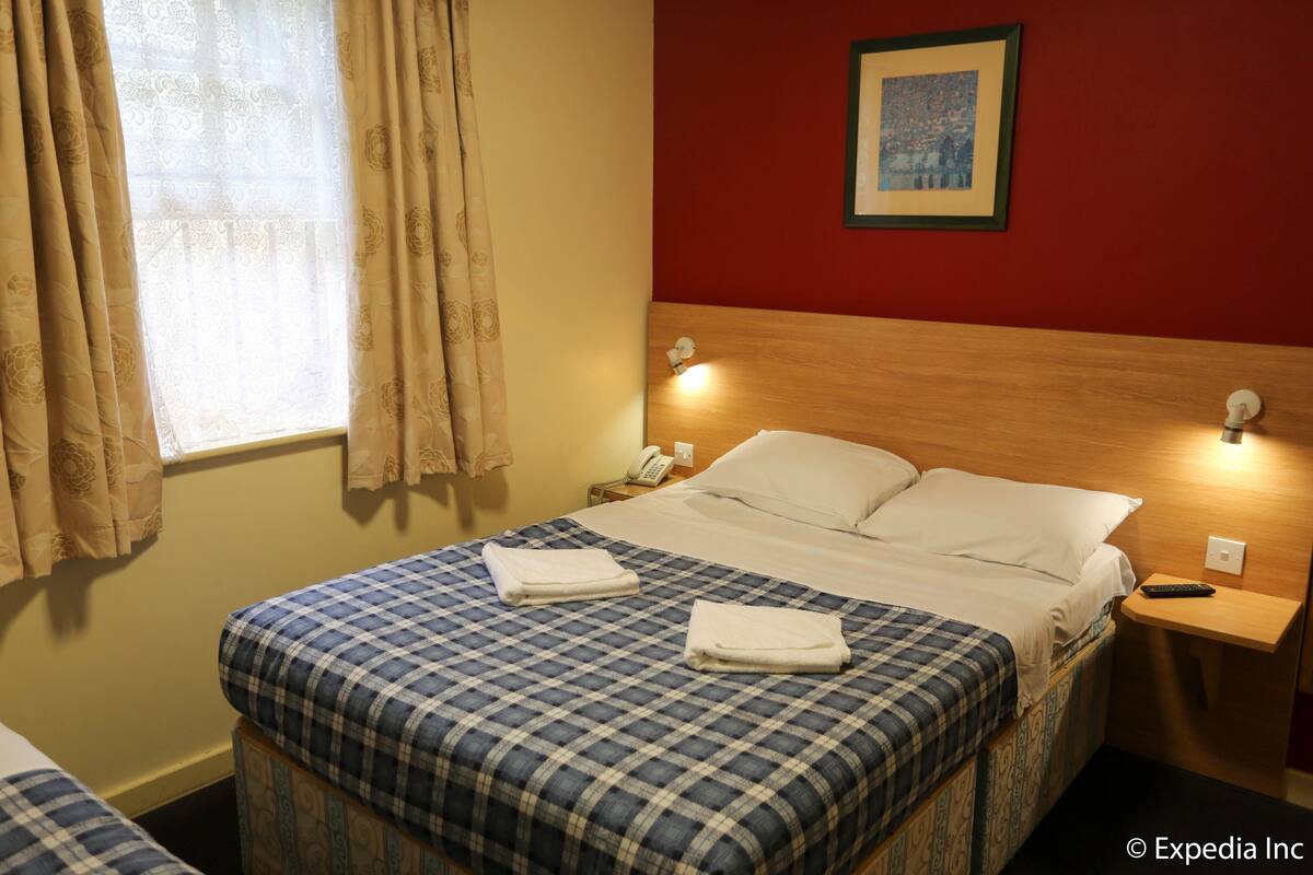 Quarto de hotel com cama, mesa de cabeceira, telefone e um quadro na parede.