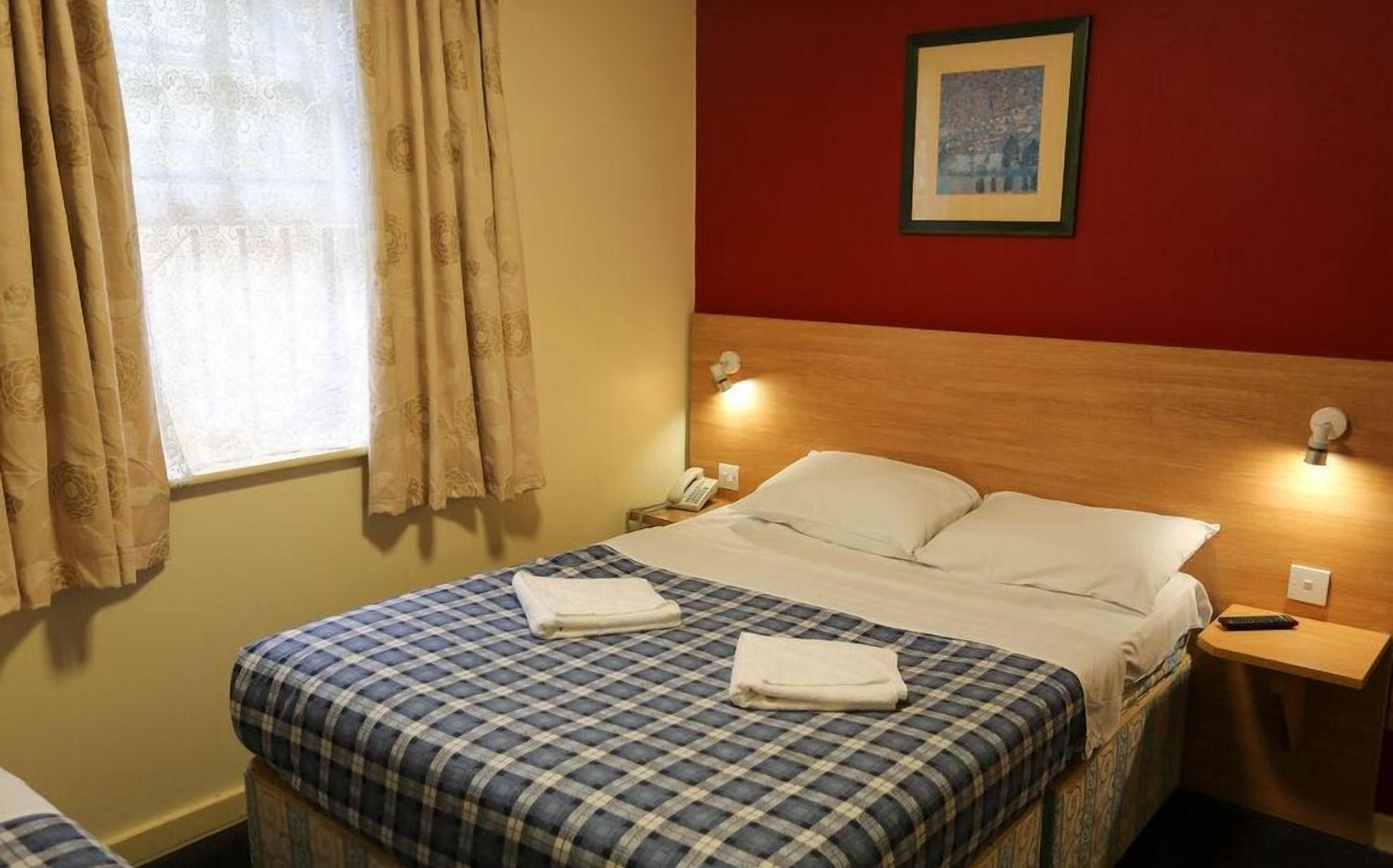 Quarto de hotel com uma cama, uma mesinha de cabeceira, um telefone e um quadro na parede.