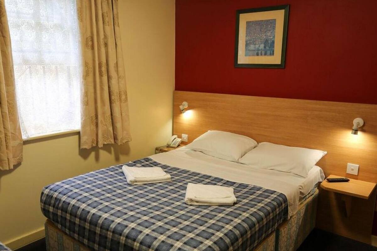 Quarto de hotel com uma cama, mesa de cabeceira, telefone e um quadro na parede.