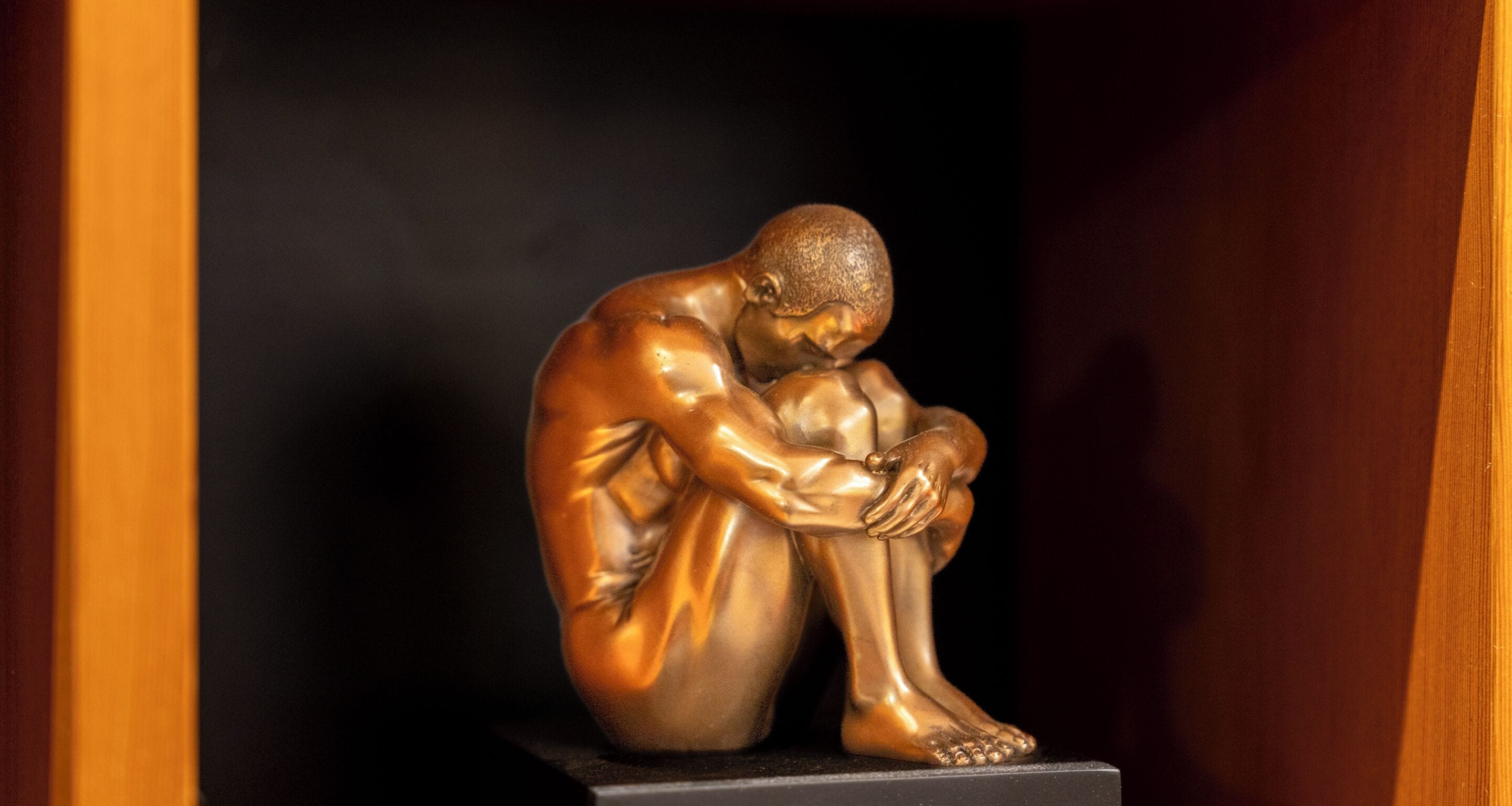 Escultura em bronze de uma figura sentada sobre um pedestal.