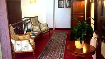 Uma sala de estar com carpete vermelho, tapete grande estampado, mesa de centro de madeira com uma planta e uma porta de madeira.