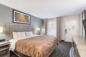 Quarto de hotel com uma cama grande, abajures, uma escrivaninha e uma porta.