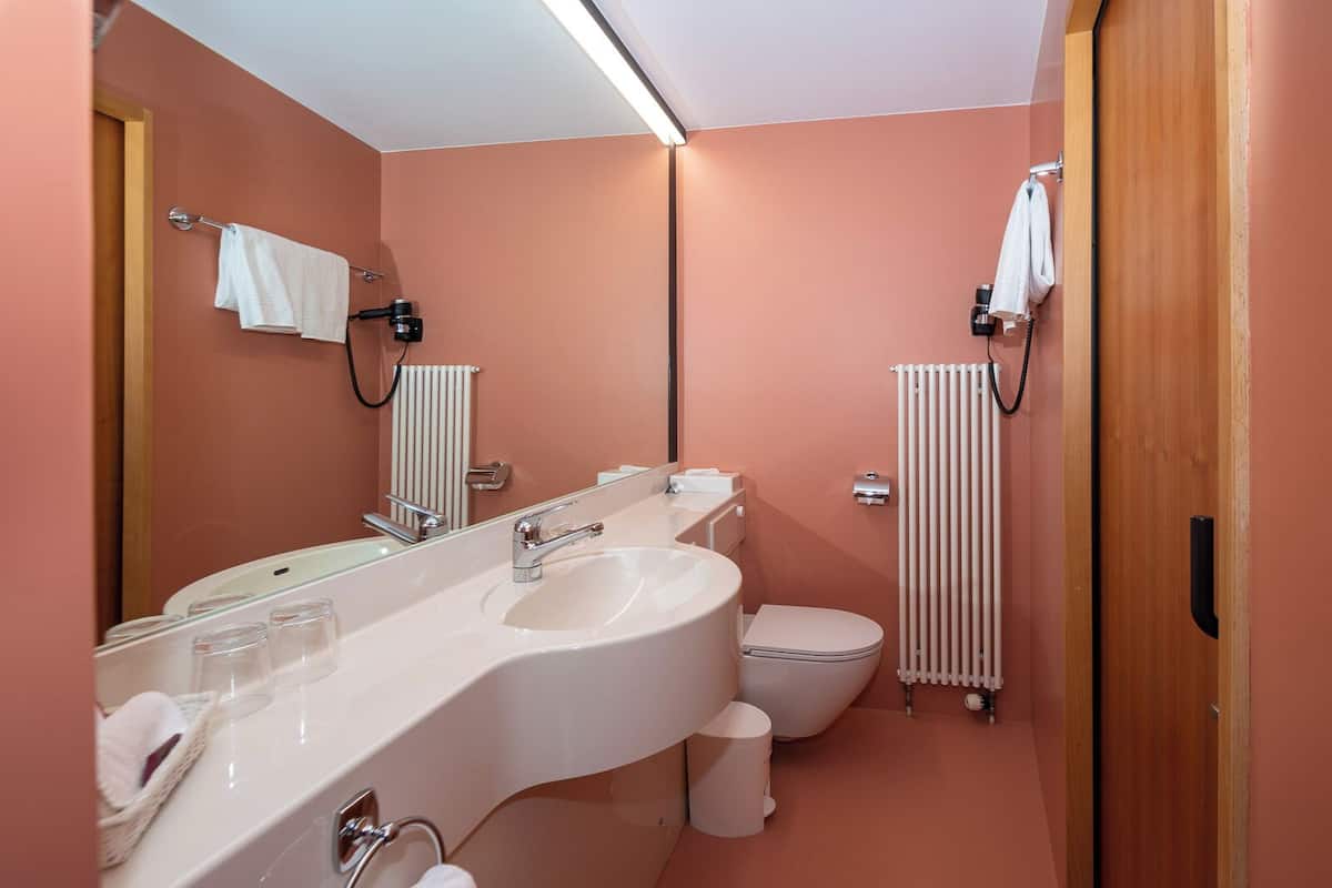 Casa de banho compacta com lavatório branco, duas espelhas, sanita e suporte para toalhas.