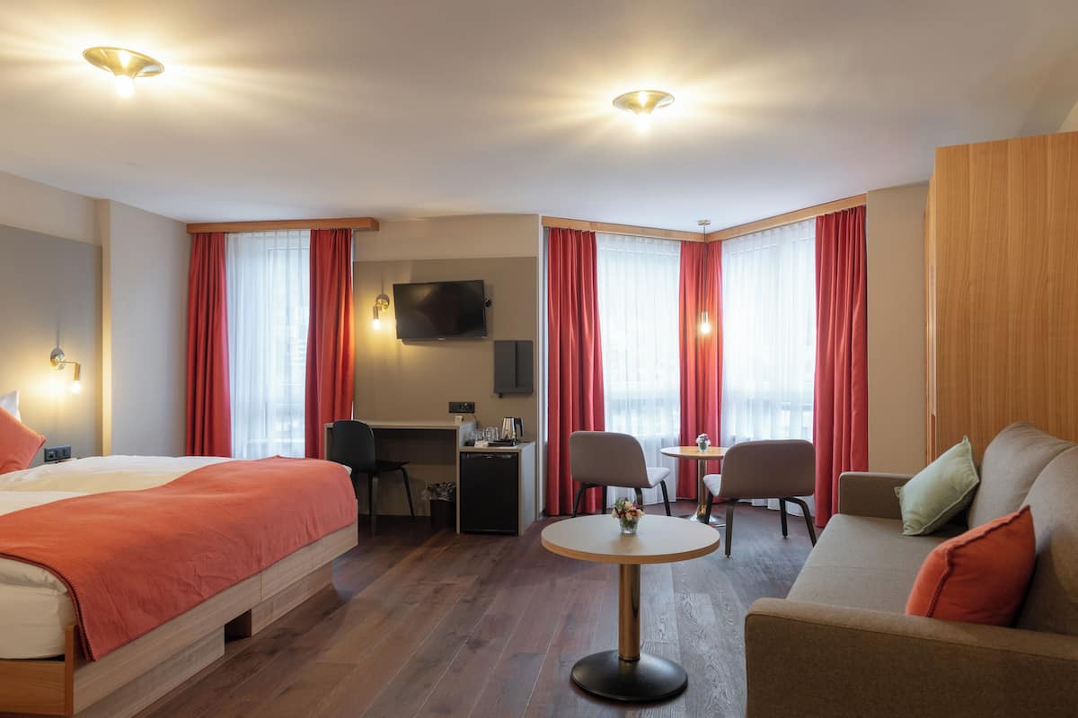Quarto de hotel com cama, escrivaninha, poltrona, sofá e uma pequena mesa.