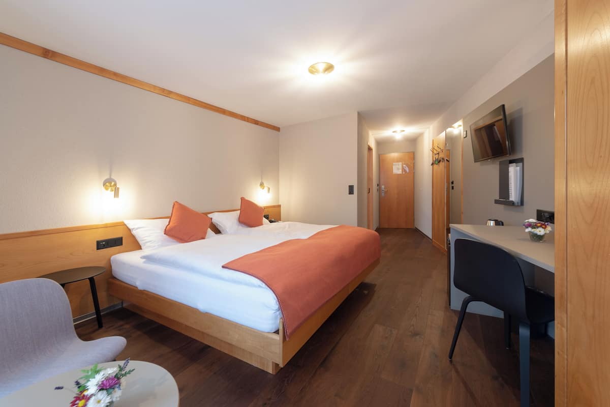 Quarto de hotel com cama de madeira, uma mesa, uma cadeira e uma TV.
