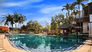 Piscina com borda azulejada, rodeada por palmeiras e um espaço coberto com assentos.