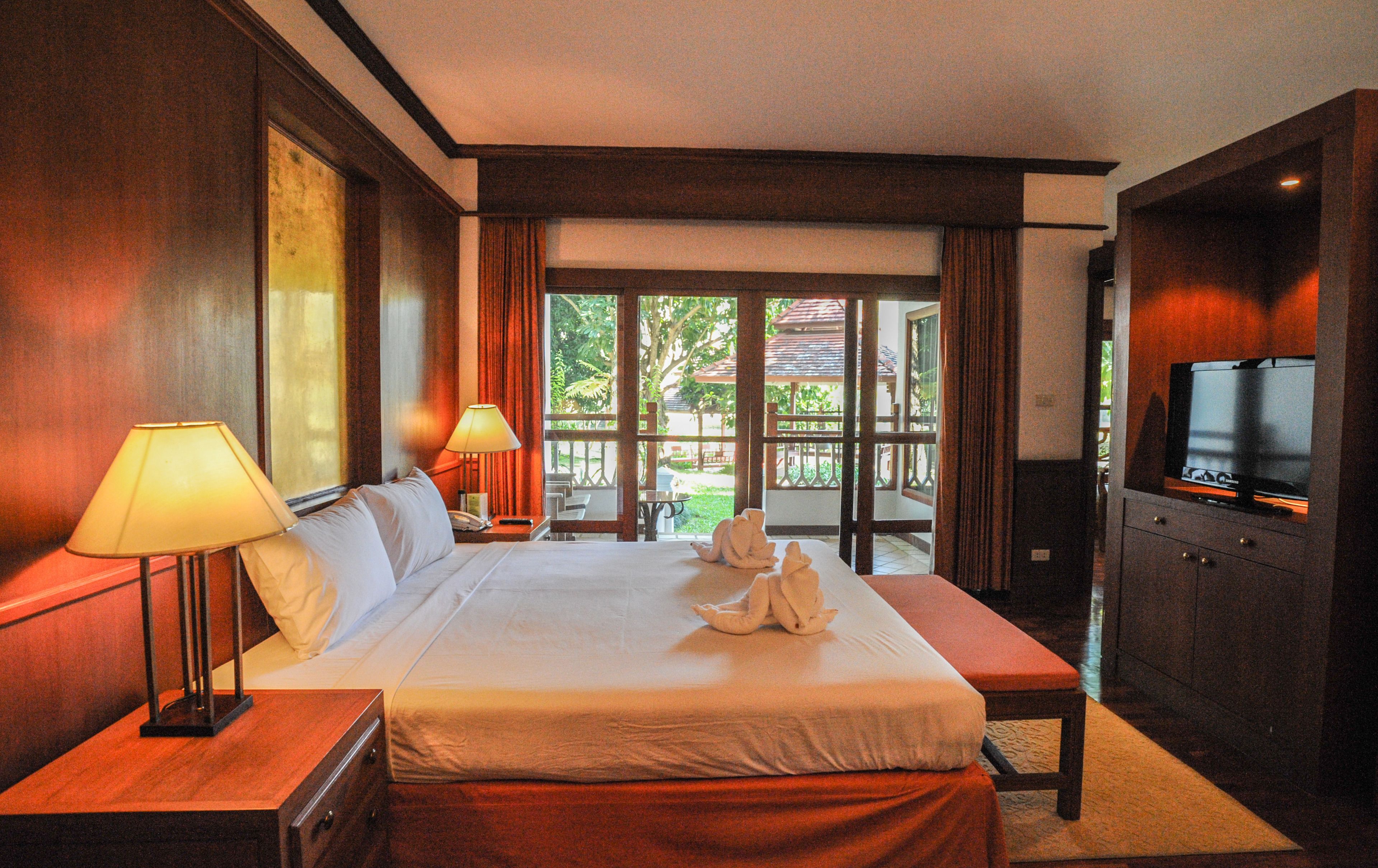 Quarto de hotel com uma cama grande, duas luminárias de cabeceira, uma TV e vista para o exterior.