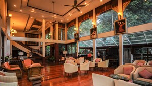 Um hall amplo com diversas áreas de estar, uma escadaria e grandes janelas com vista para o exterior.