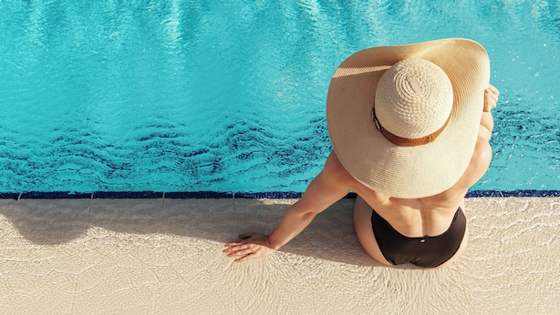 Uma pessoa sentada à beira da piscina, com vista para a água.