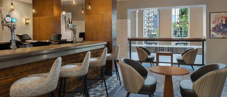 Uma área de bar com banquetas, balcão e uma área de estar com mesa redonda e cadeiras.
