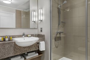 Casa de banho moderna com bancada de granito, lavatório branco e área de duche com divisória de vidro.