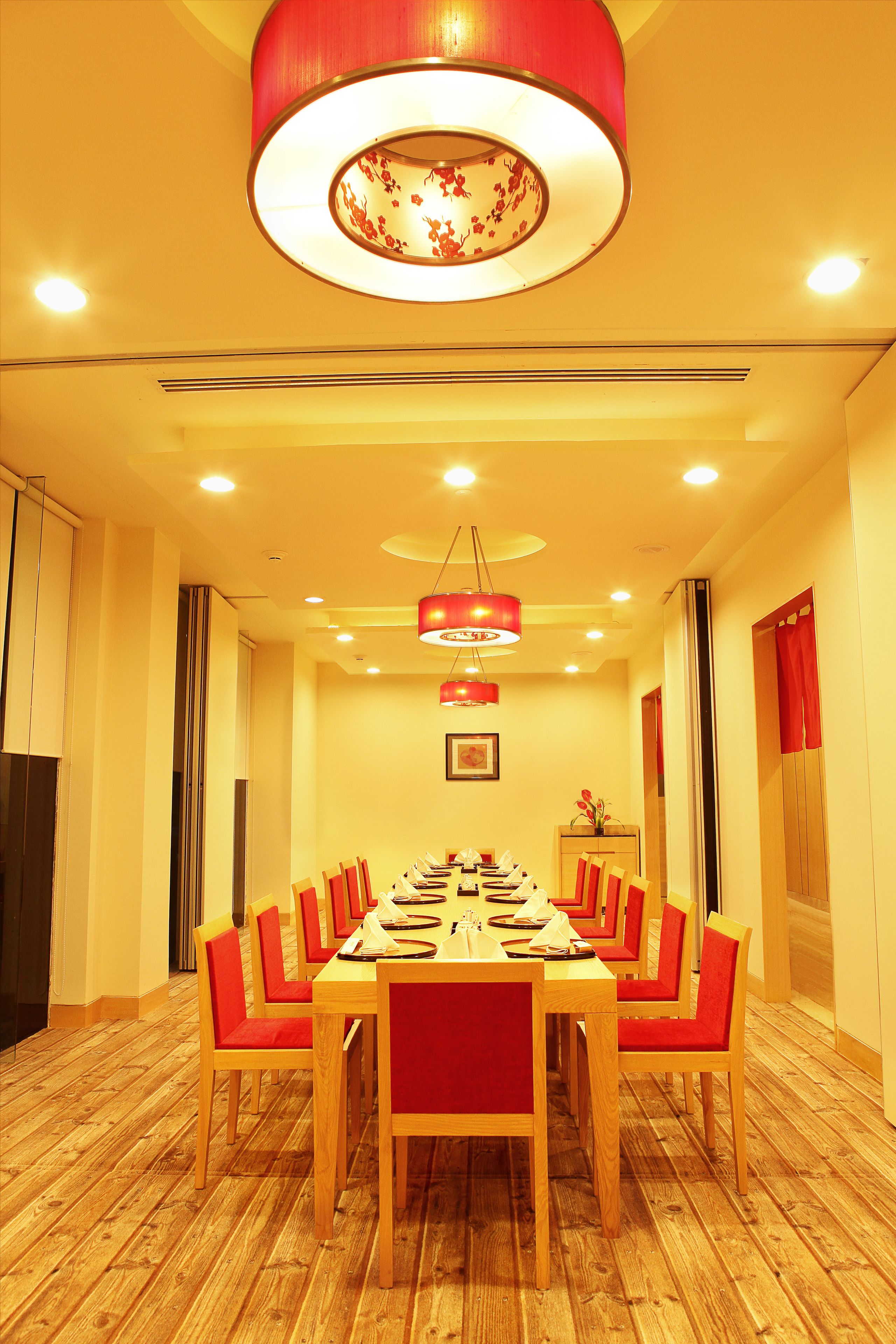 Uma sala de conferência com uma mesa comprida, cadeiras vermelhas e um lustre central.