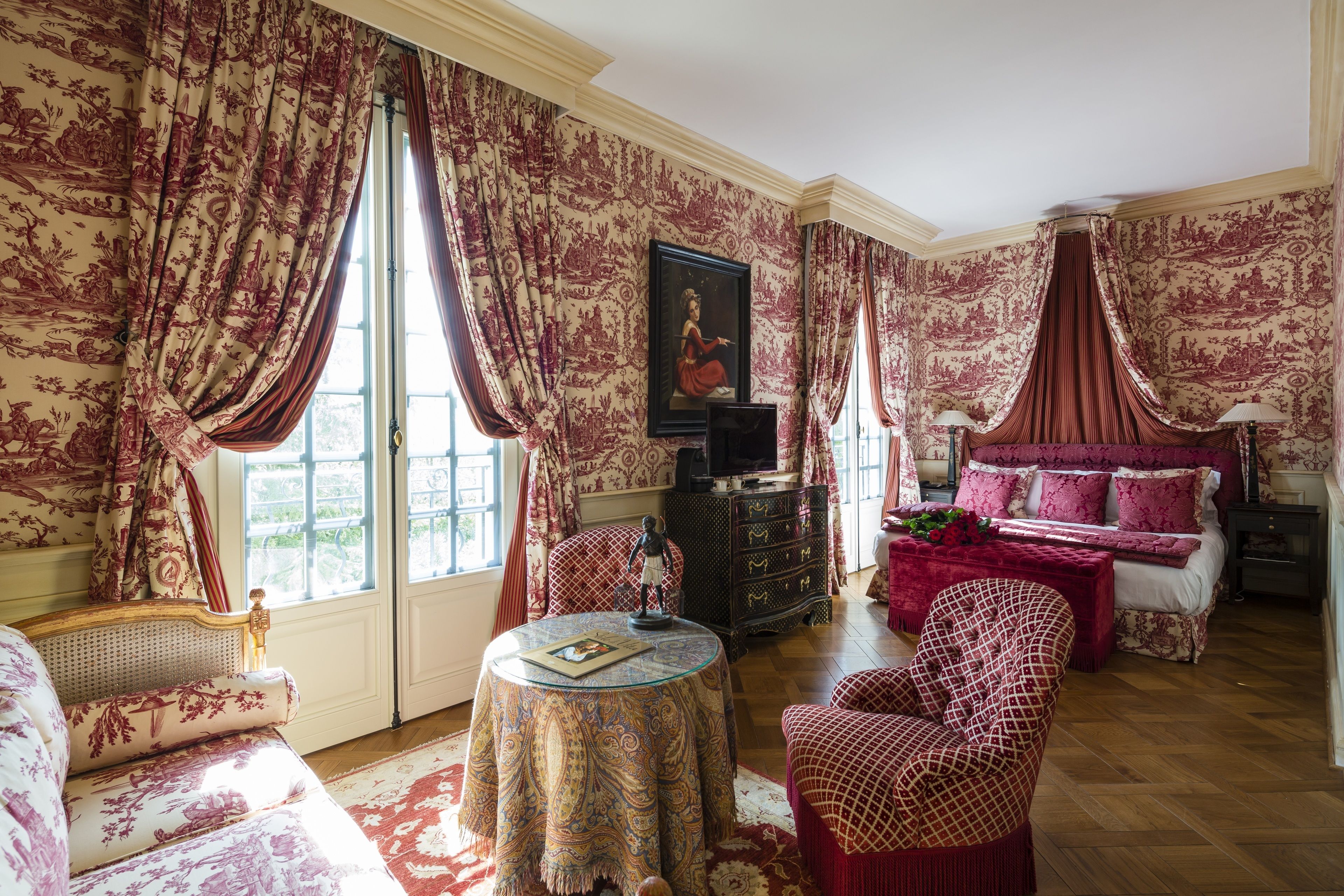 Um quarto com uma janela grande, uma cama, uma cadeira, uma mesa e um aparador.